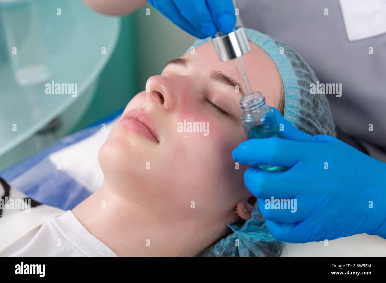 Hands of cosmetologist dripping nourishing oil facial skin of young ...