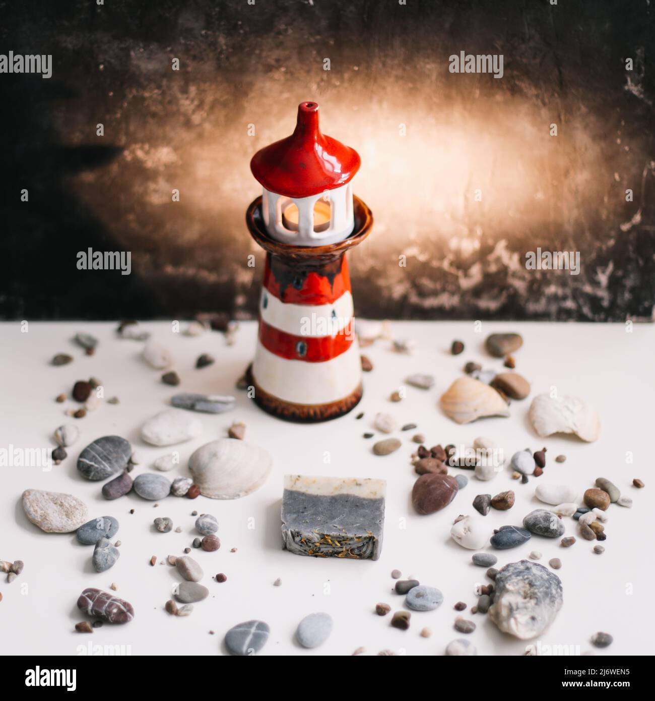 A small decorative lighthouse with sea shells and stones on a dark ...