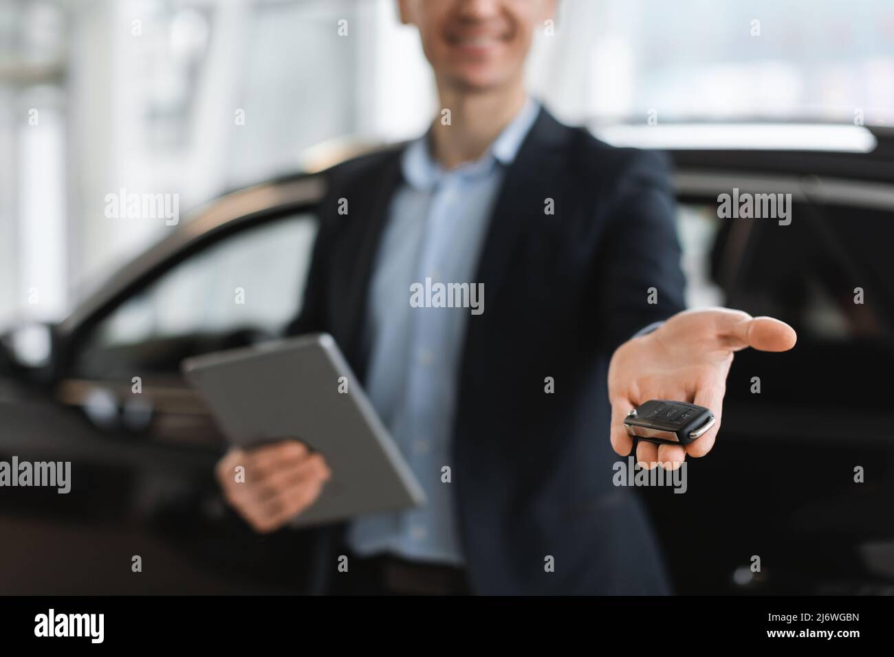 Cropped view of young salesman showing car key in modern dealership ...