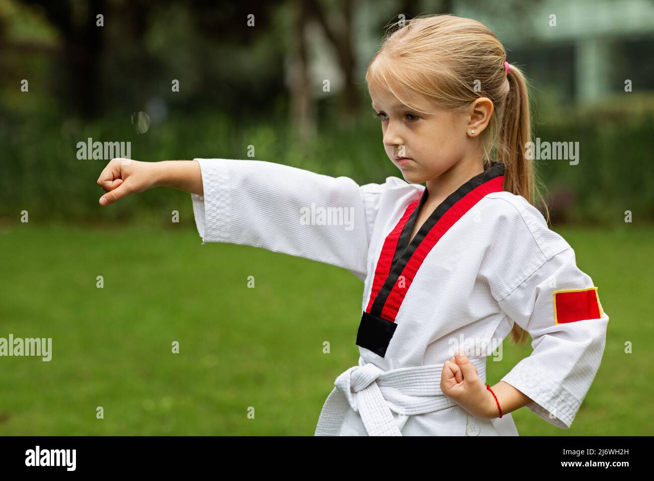 Caucasian little girl six years old in kimono with white belt exercising Taekwondo at summer ...
