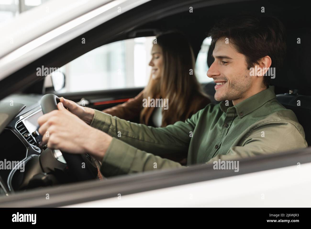 Cheerful young Caucasian couple test driving new car at auto dealership ...