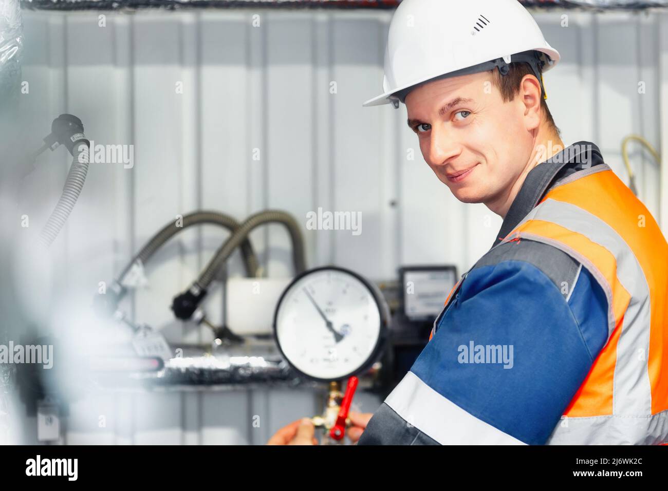 Gas boiler room operator in helmet and work clothes looks into camera ...
