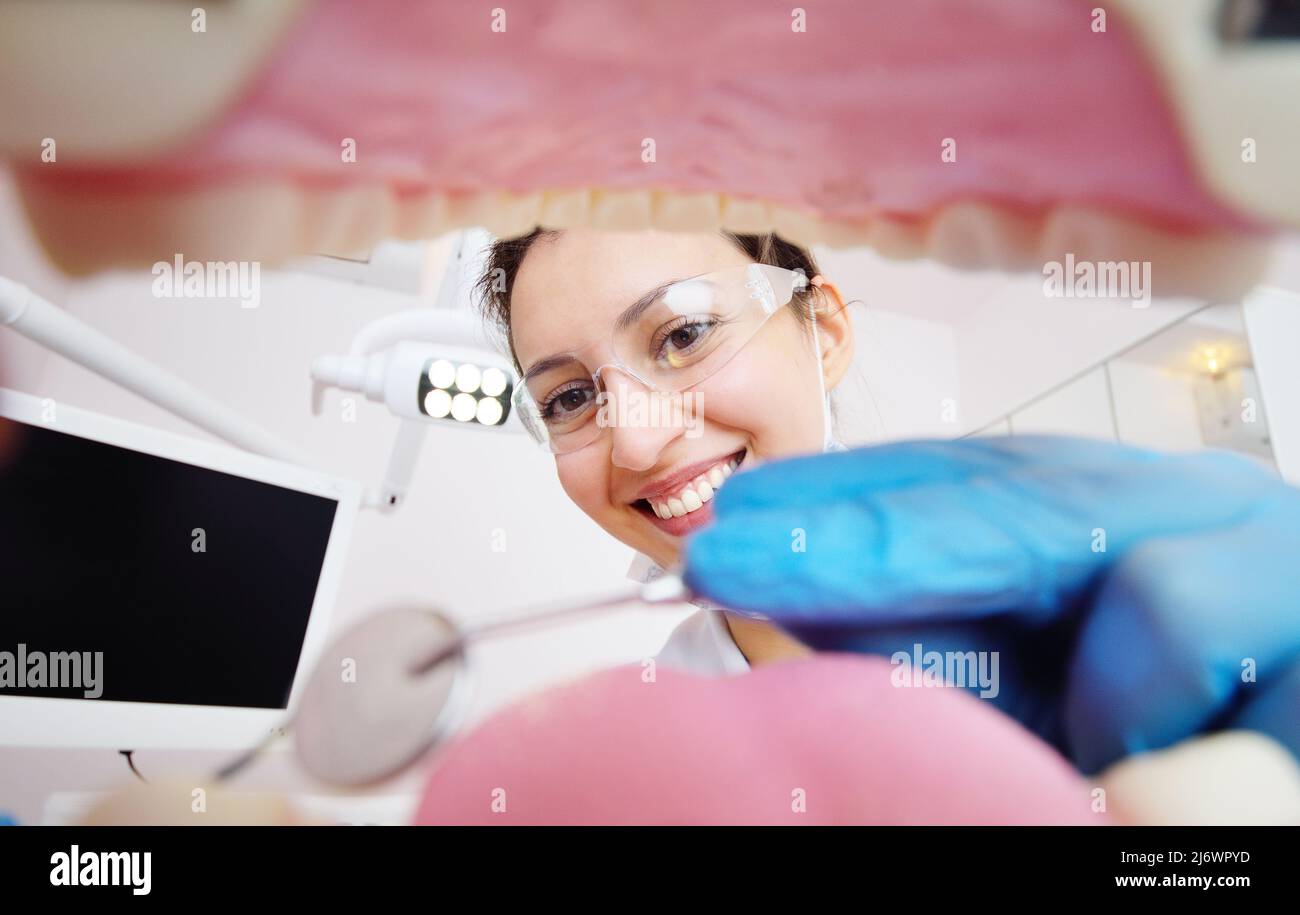pretty young female dentist examines the patient's teeth. View from ...