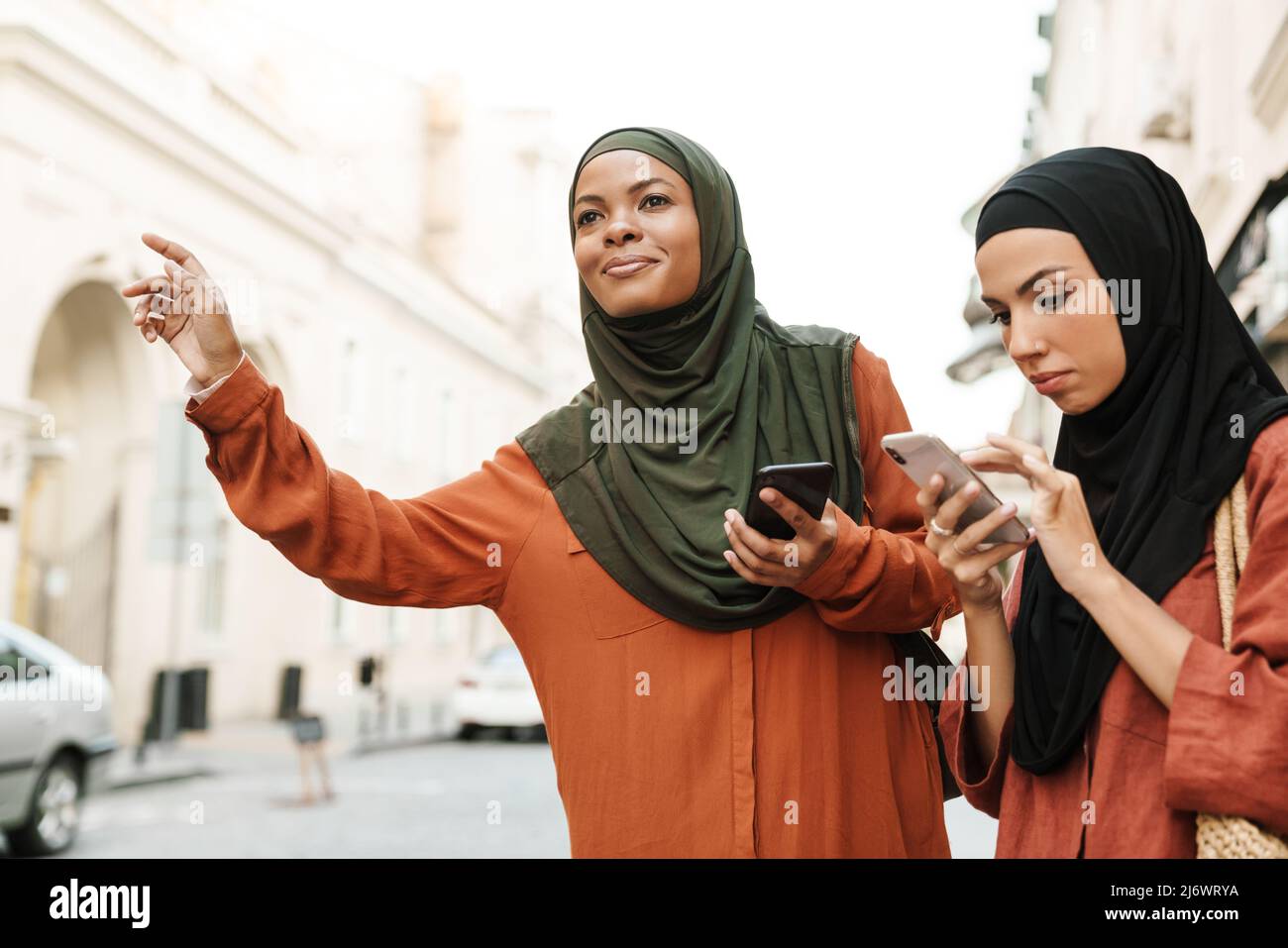 Multiracial muslim women using mobile phone and waving hand for taxi on ...