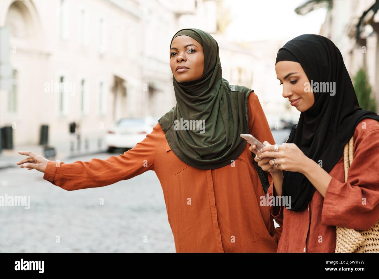Multiracial muslim women using mobile phone and waving hand for taxi on ...