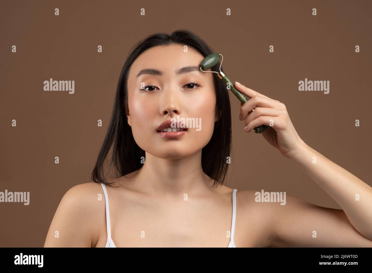 Beautiful asian lady using jade face roller on her flawless skin ...