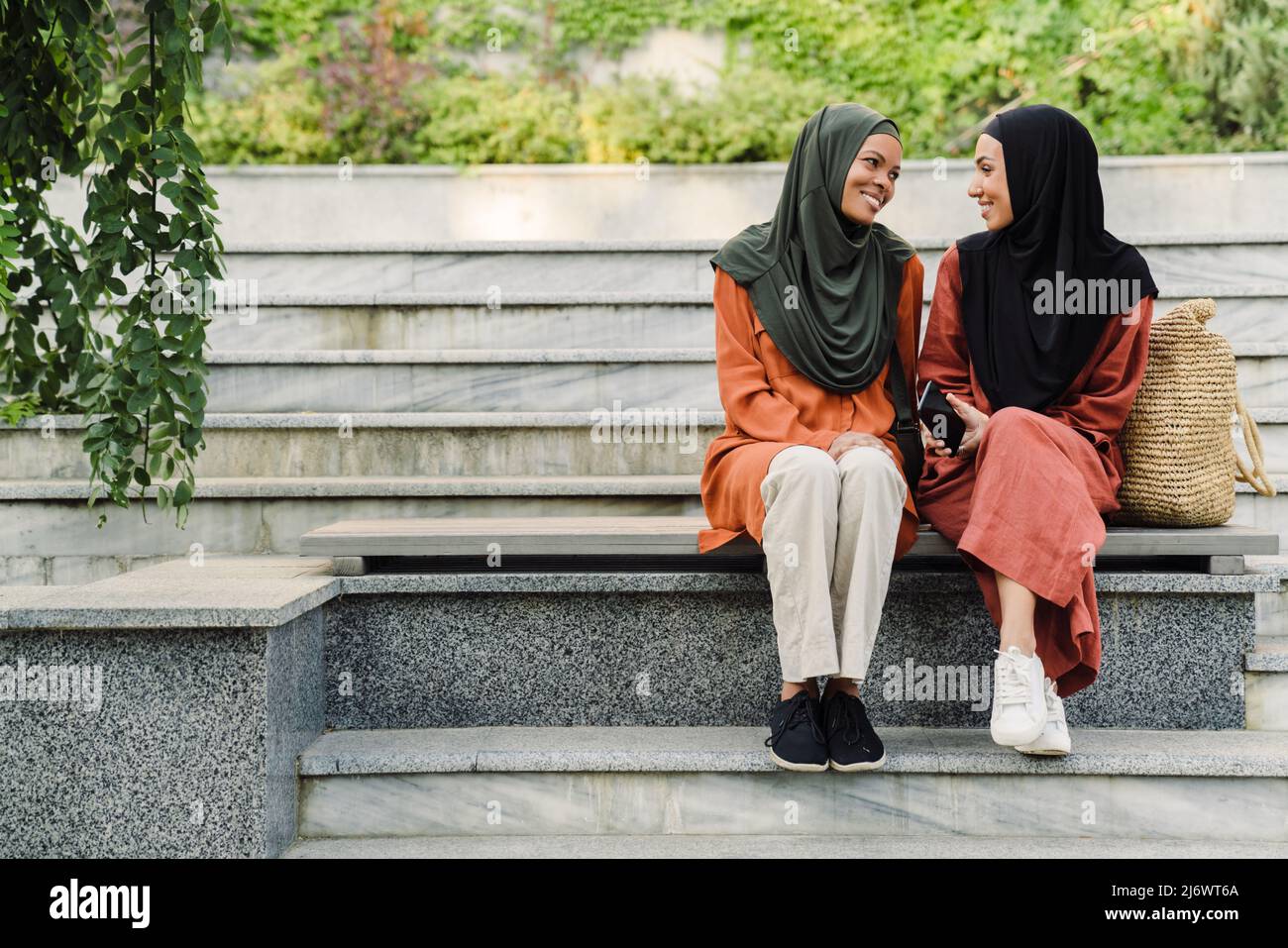 Multiracial muslim women talking and smiling while sitting on bench ...