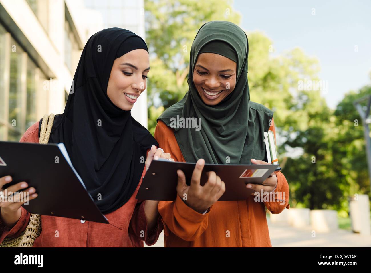 Multiracial muslim women examining documents together while standing on ...