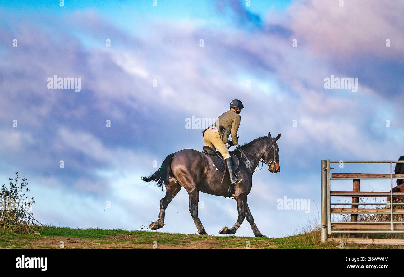 A rider galloping across the skyline on a horse against a stormy sky ...