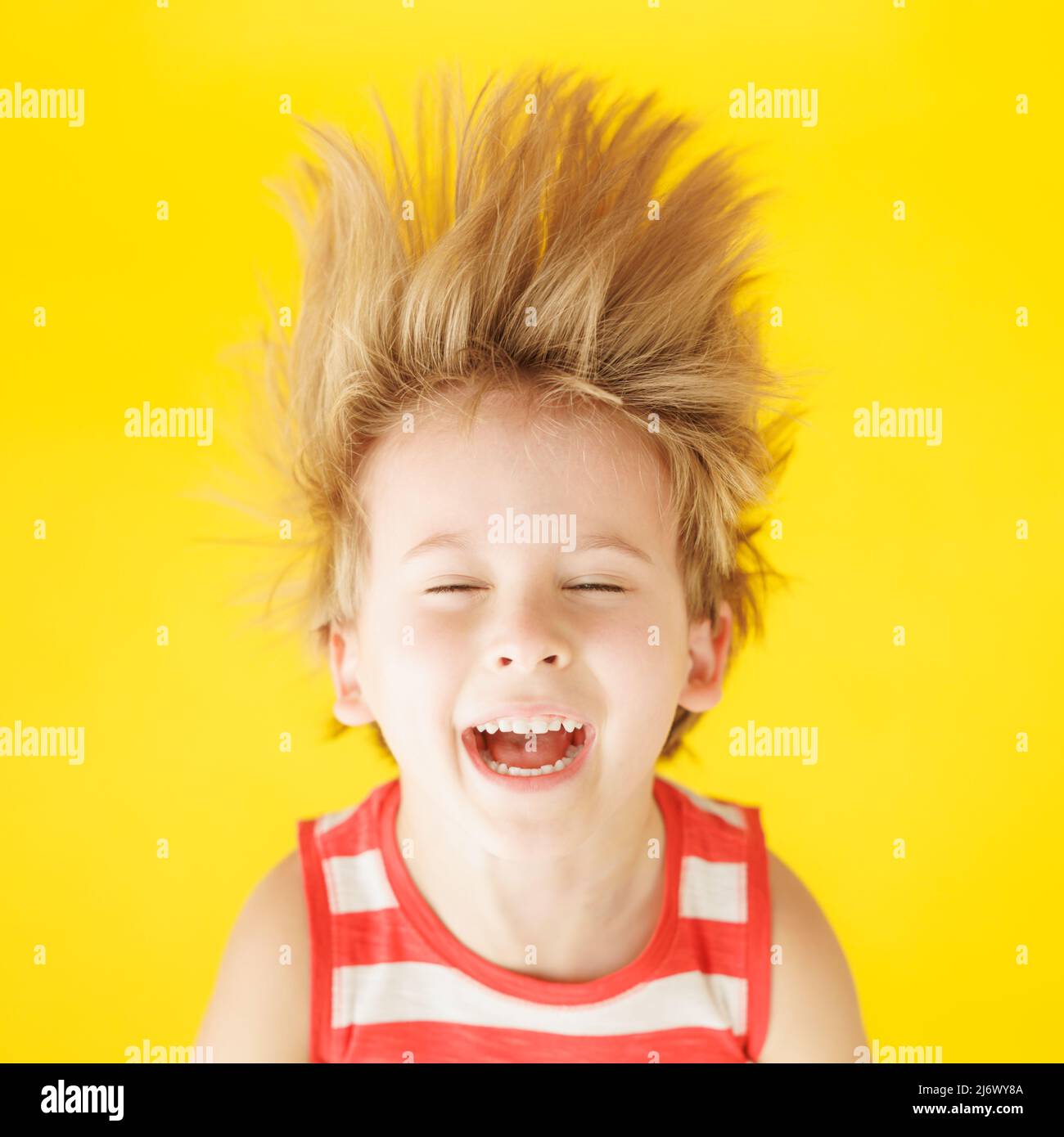 Happy child shouting against yellow paper background. Funny kid hanging ...