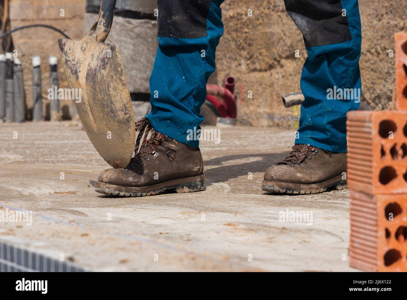 Worker's legs working in construction site with a shovel resting on ...