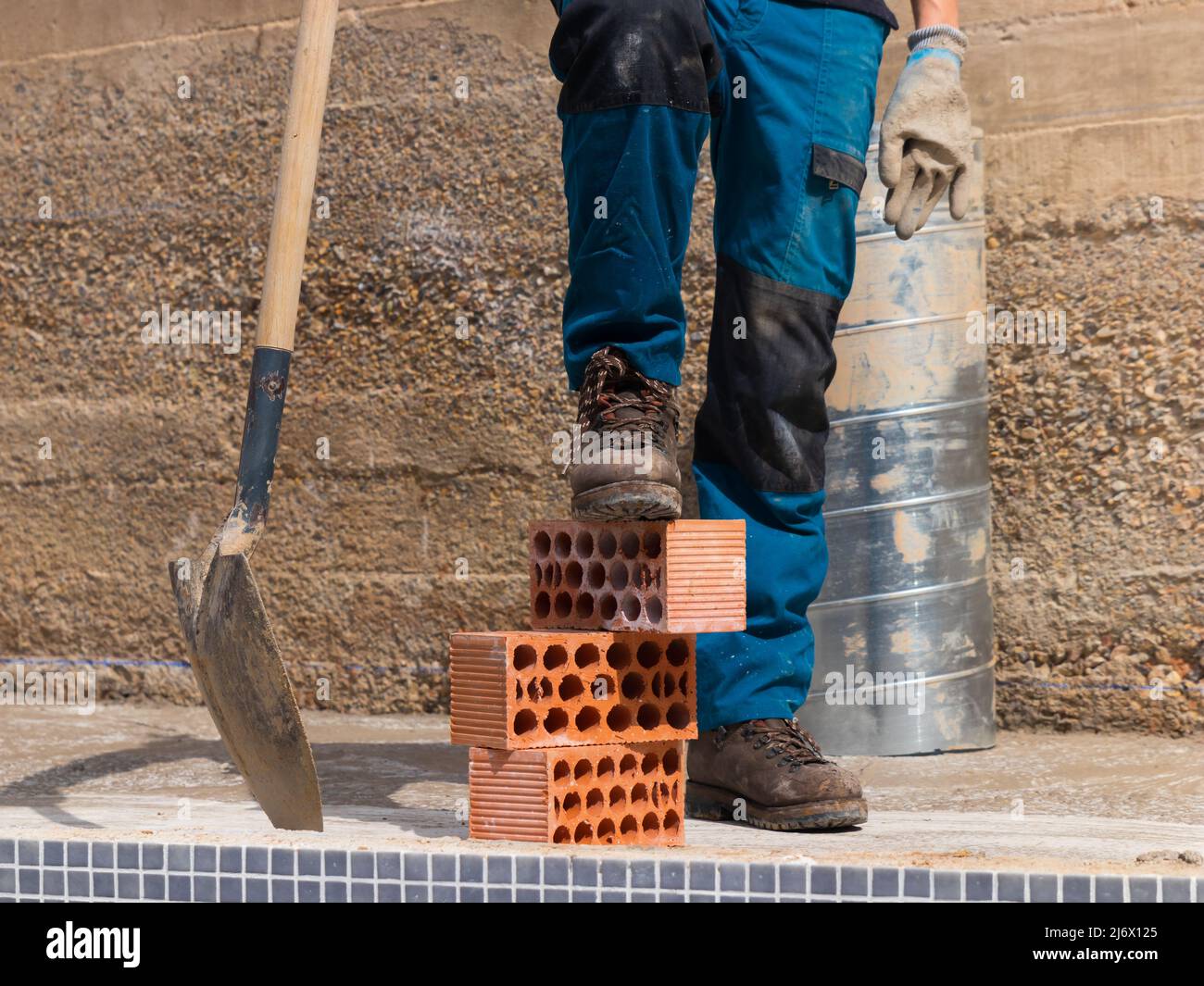 Legs of construction worker with foot on orange bricks and shovel in ...