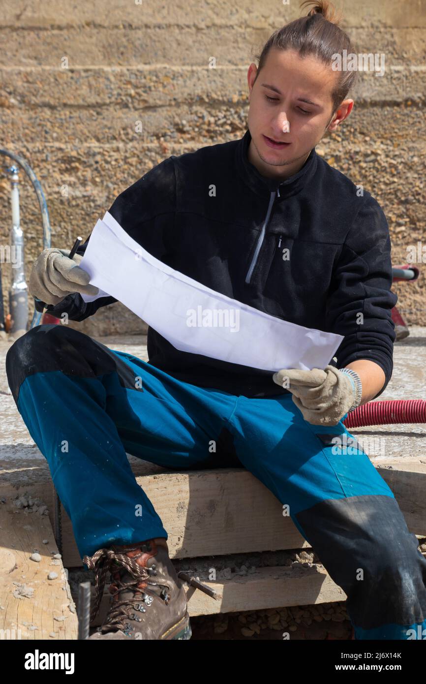 Young Laborer aprentice reading and holding a plan in construction site ...