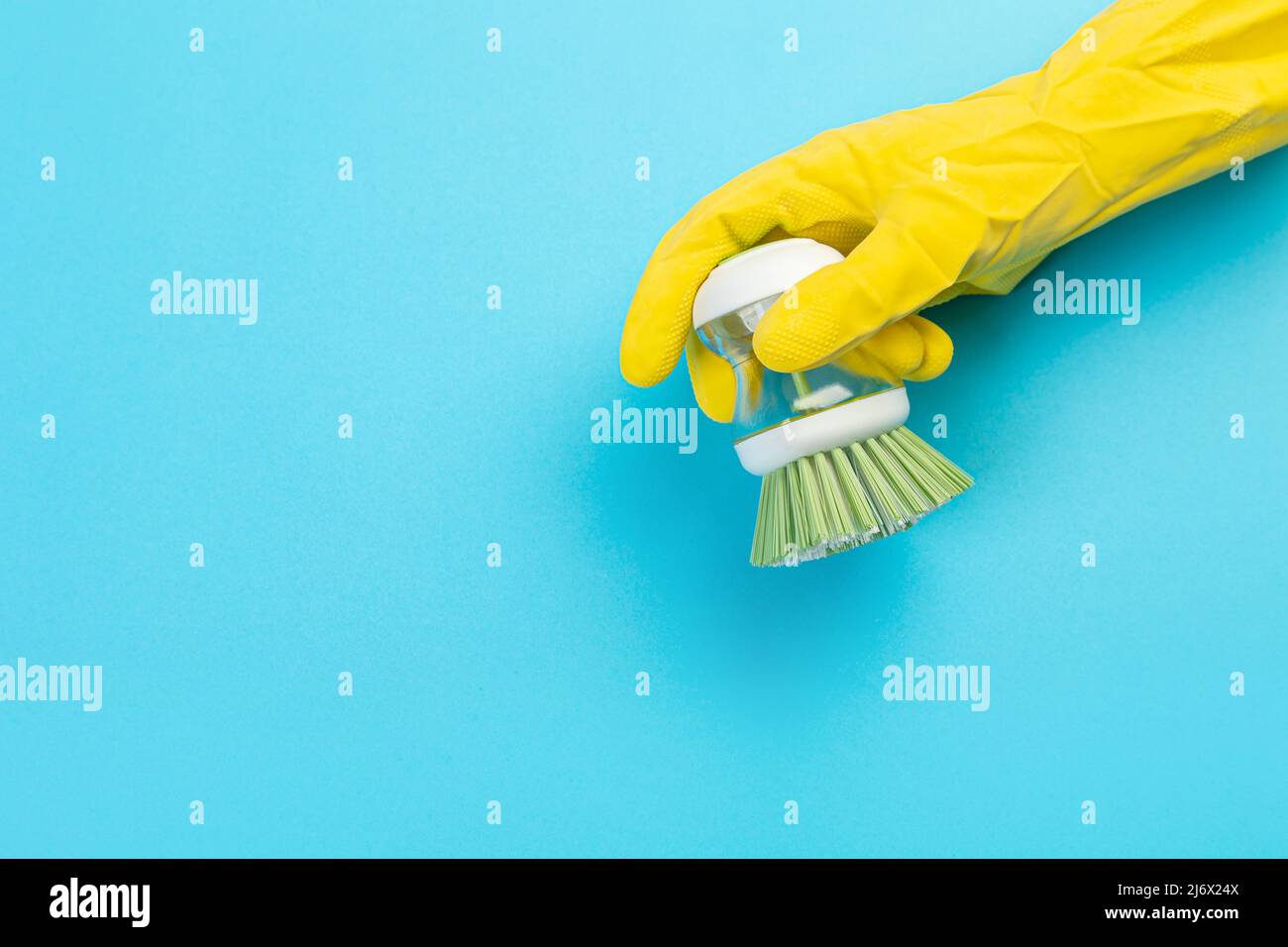 A hand in a yellow glove holds a plastic cleaning brush on a blue ...