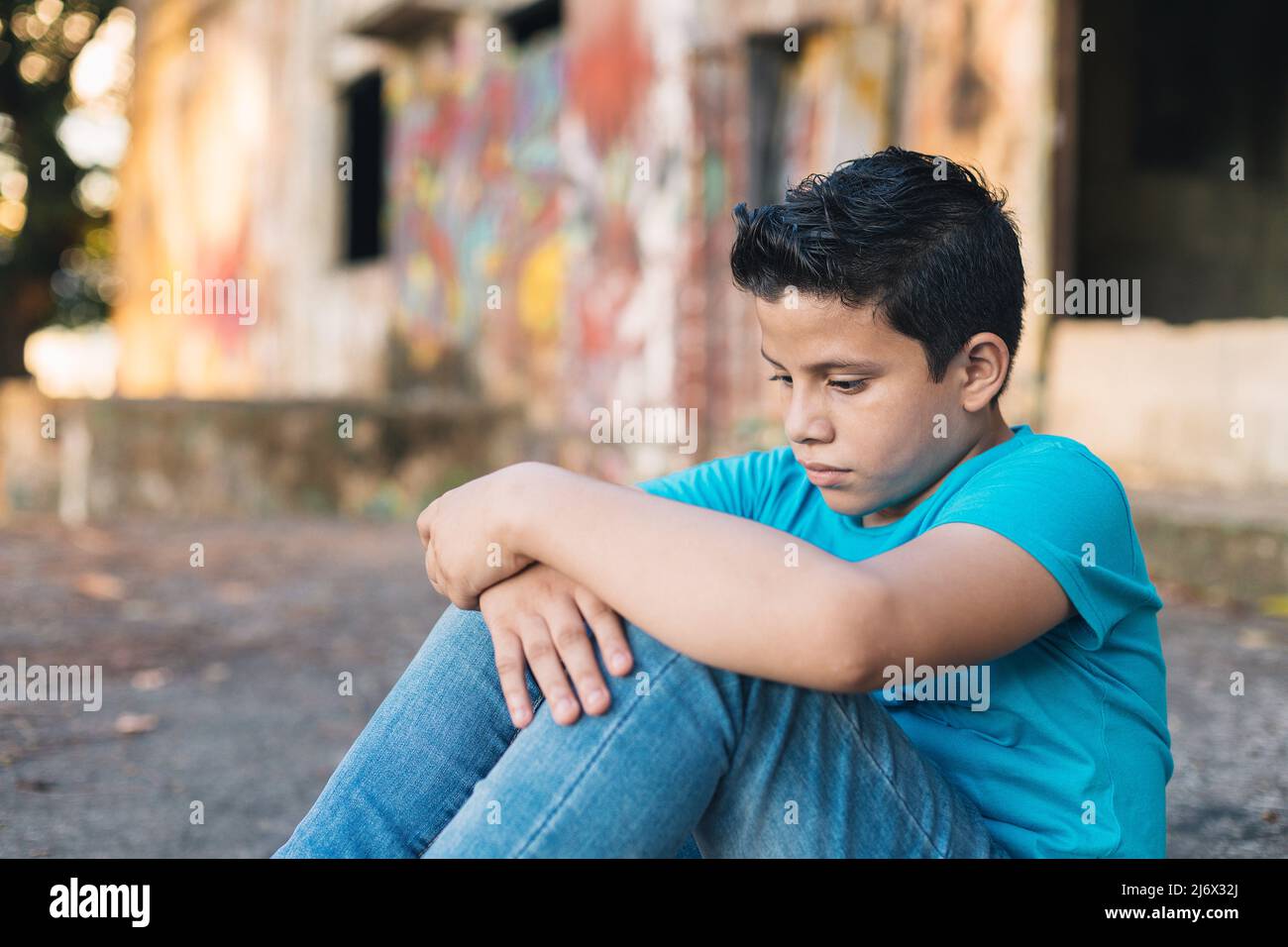 Hispanic boy sitting on some ruins looking at the horizon, with a sad ...
