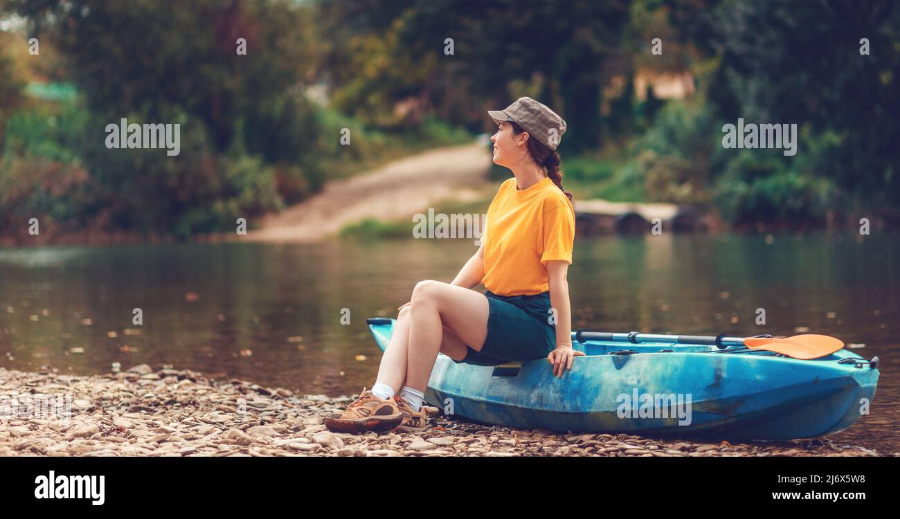 Banner. A young smiling woman is sitting on a blue kayak and looking at ...