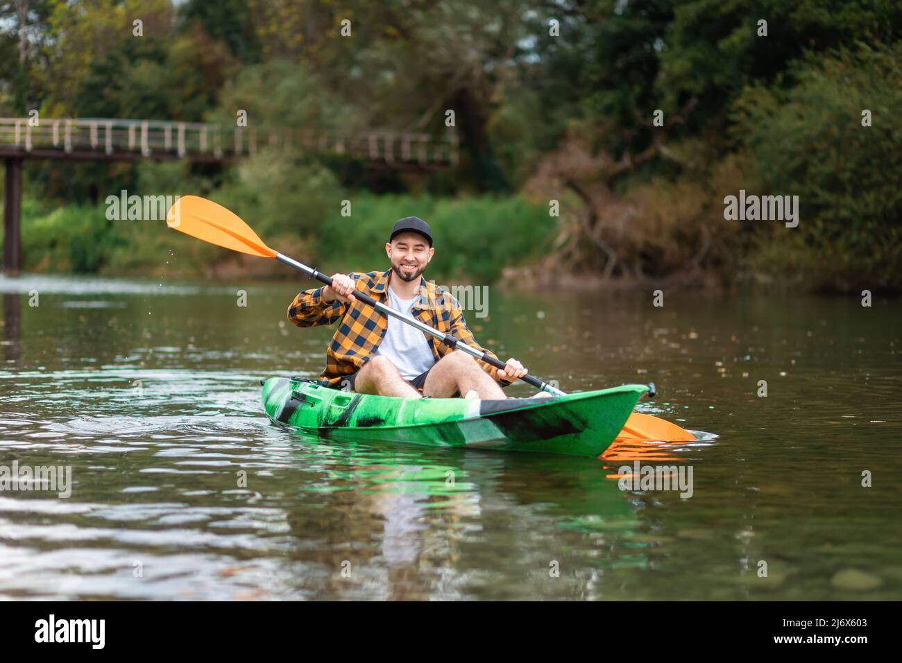Happy bearded caucasian man in shirt and cap kayaking at the river with ...