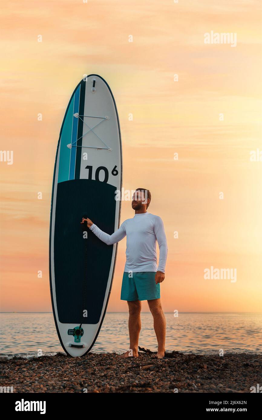 Extreme activity. Fit man holding a sup board and posing on the beach ...