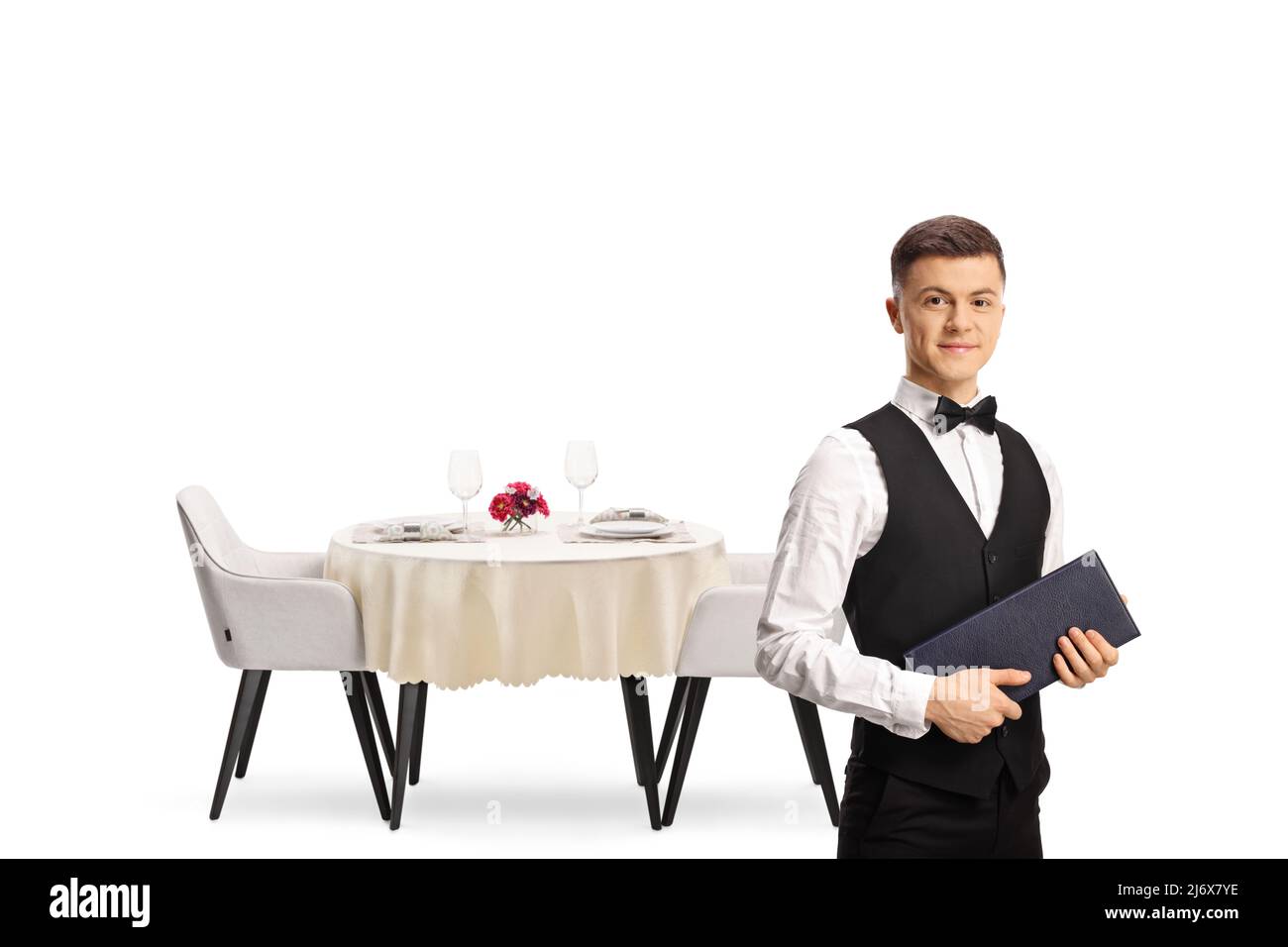 Young waiter with a bow tie standing in front of a table and holding a ...