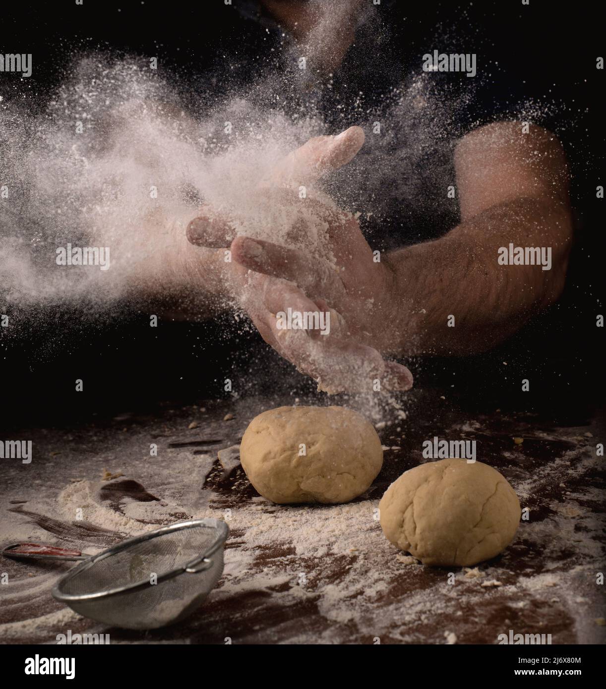 Explosion of flour in male hands and dough on a dark background. Dough ...