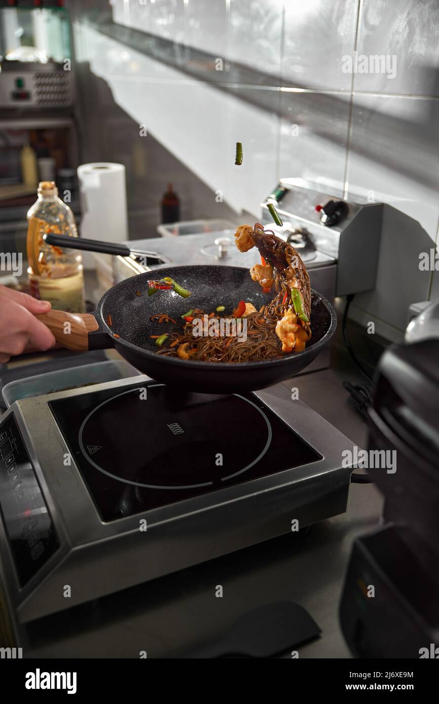 Chef hand keep wok. Closeup hands tossing food at professional dark ...