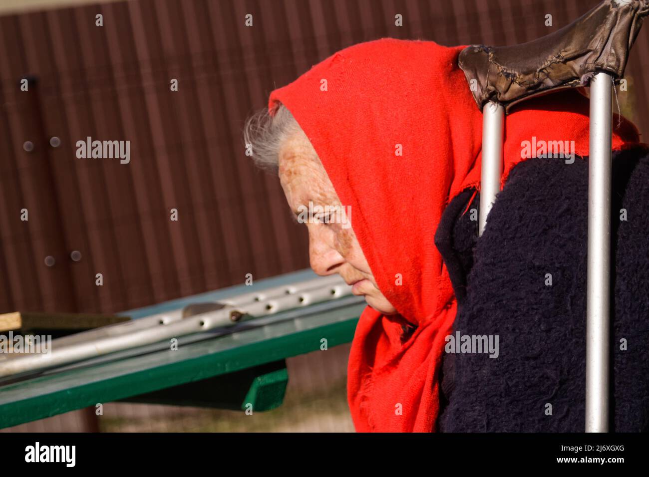 Defocus ukrainian elderly woman in red shawl with crutches sitting ...