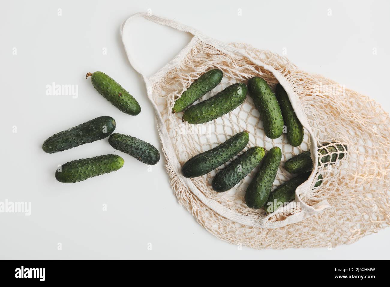 Green fresh cucumbers in a string bag isolated on white background ...