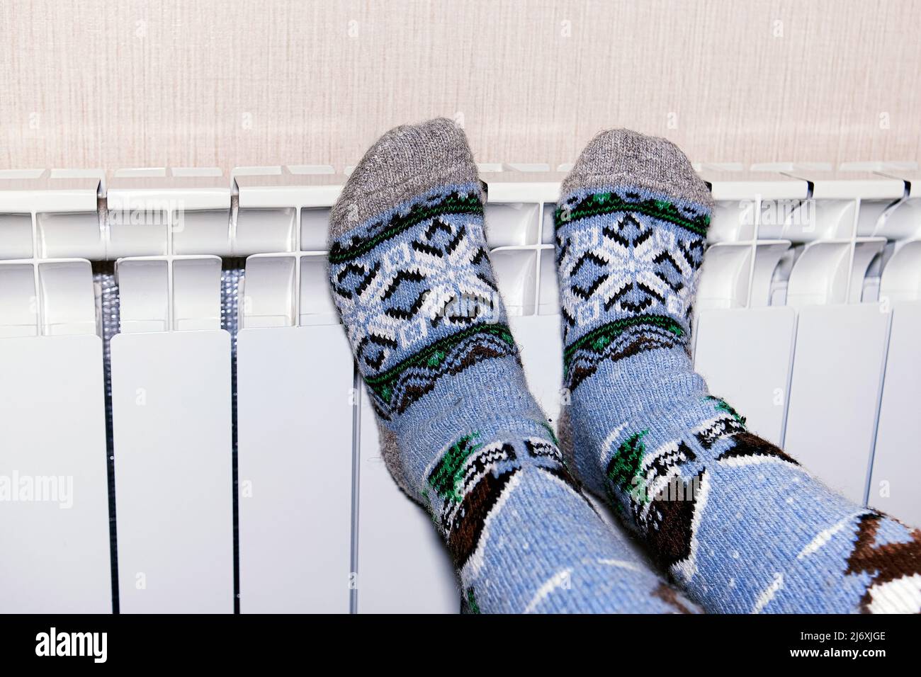 A woman warms her frozen feet in socks on a battery. The concept of ...