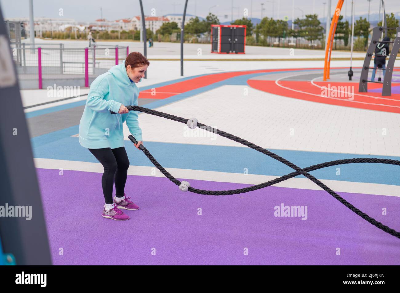Caucasian woman in a mint sweatshirt is training with battle ropes at ...