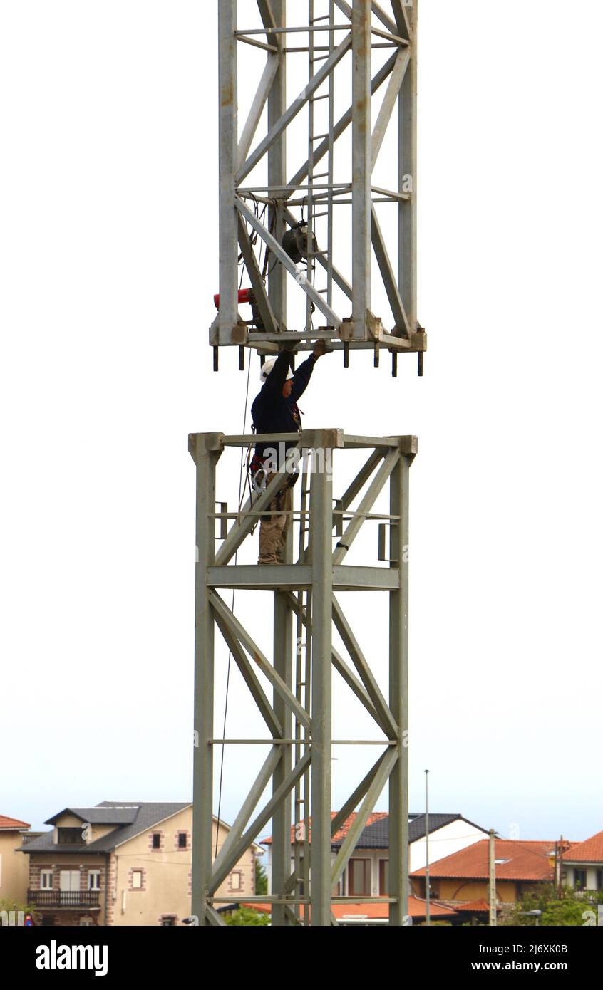 A construction worker guiding the second section of mast of a tower ...