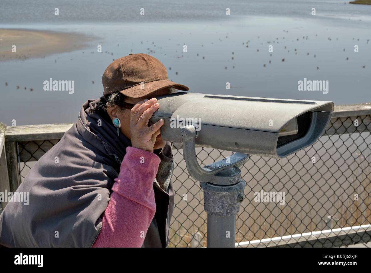 A woman of color gazes through a pair of tourist binoculars from the ...