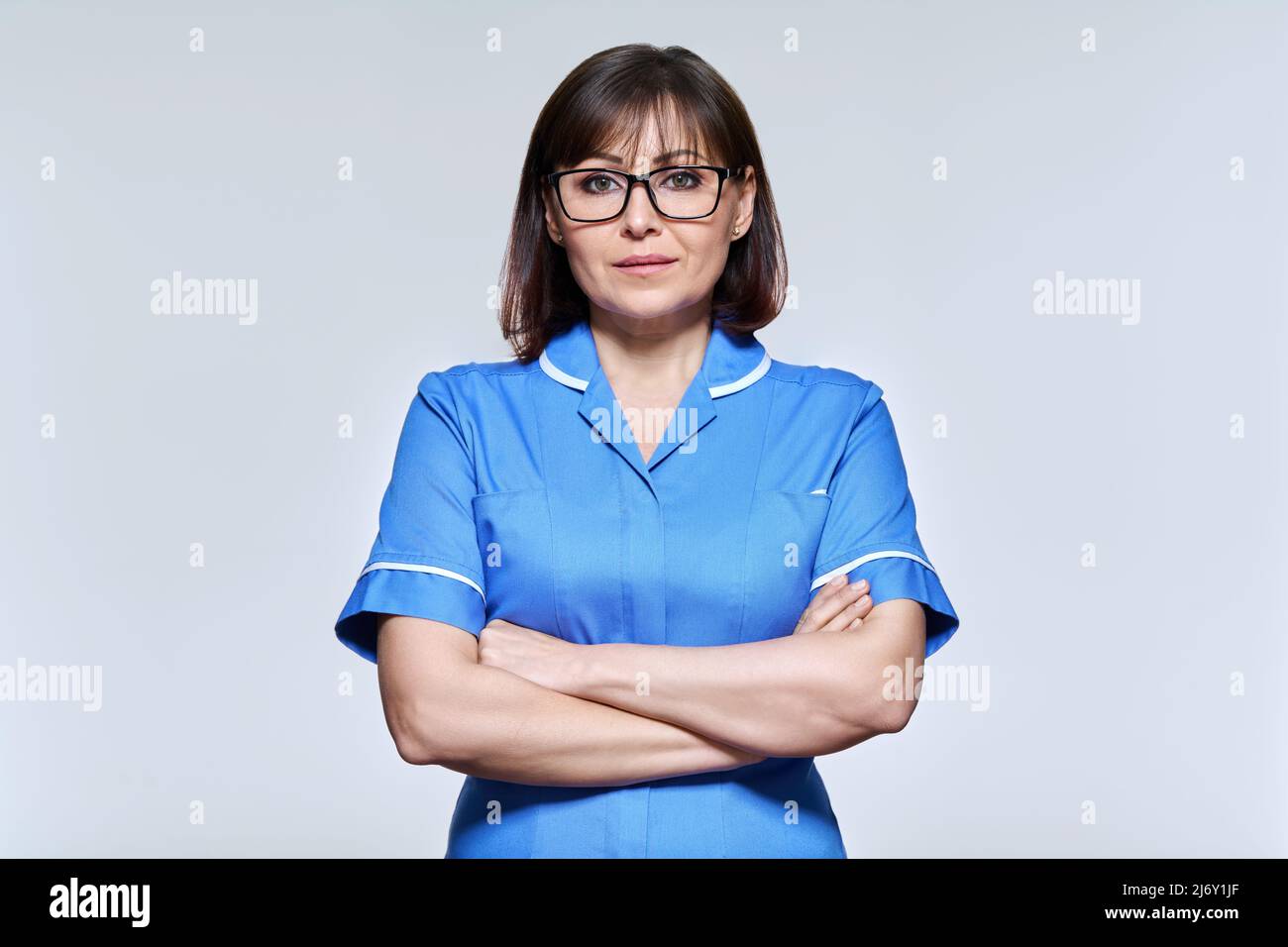 Portrait of middle aged nurse in blue uniform looking at camera on ...