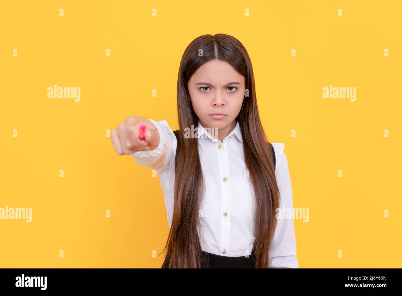 Serious frown school girl point pen putting out hand yellow background ...
