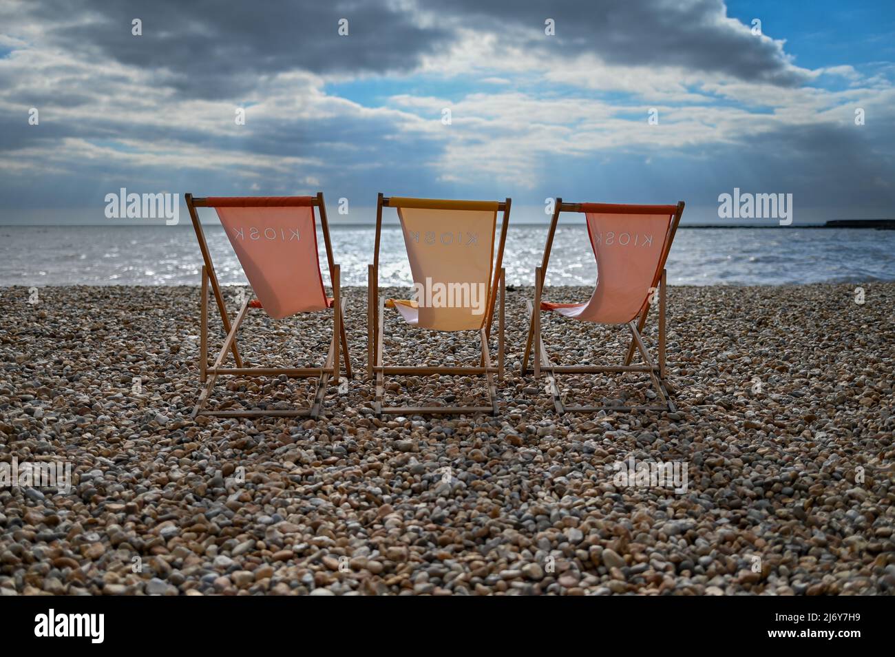 three deck chairs on British pebble beach on coastline looking in to ...