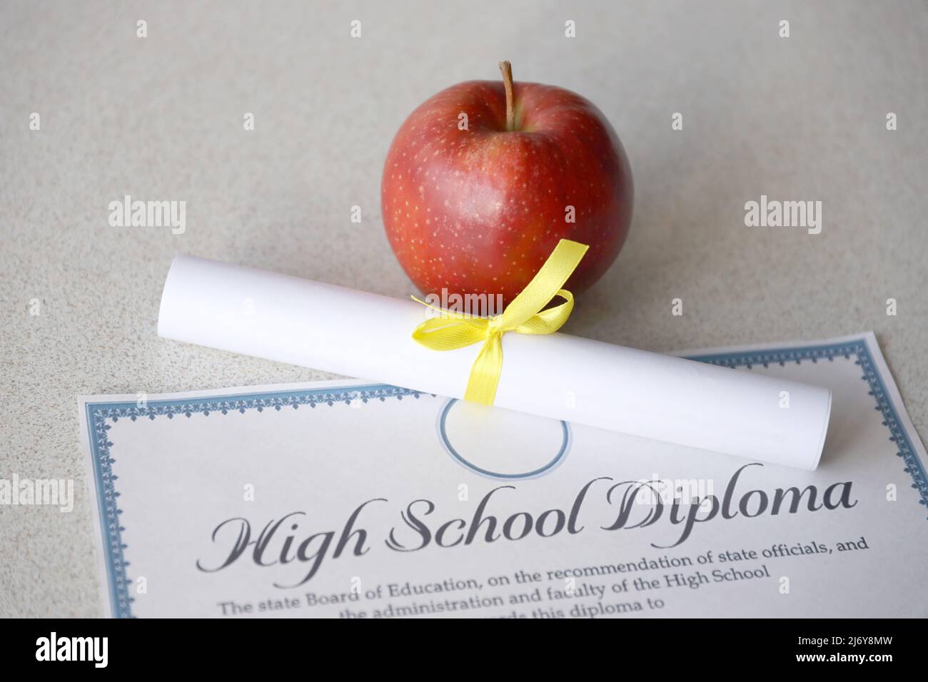 A high school diploma lies on table with small scroll and red apple ...