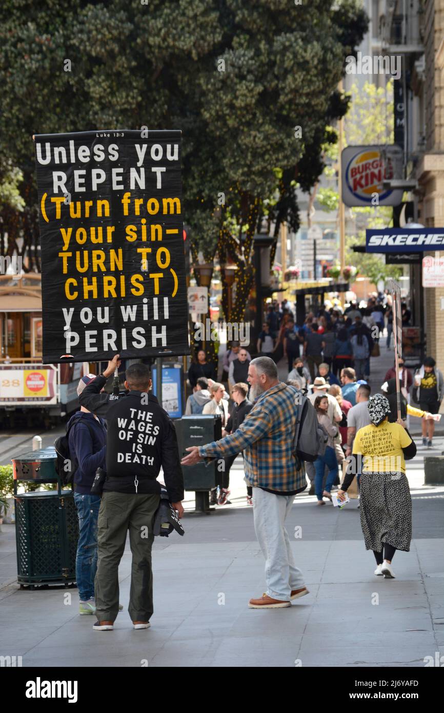 Evangelical Christians with signs and a megaphone walk along a sidewalk ...