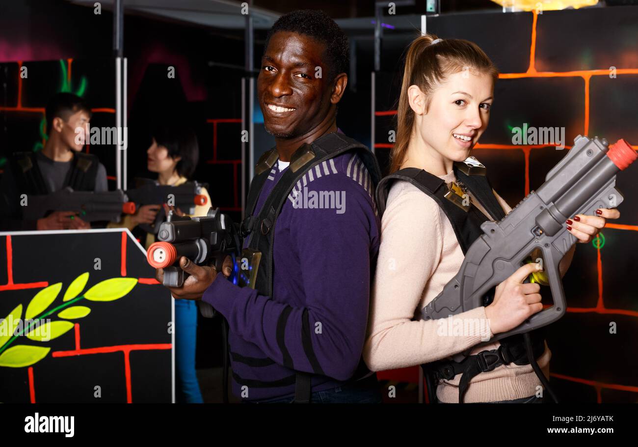 Smiling laser tag players standing back to back Stock Photo - Alamy