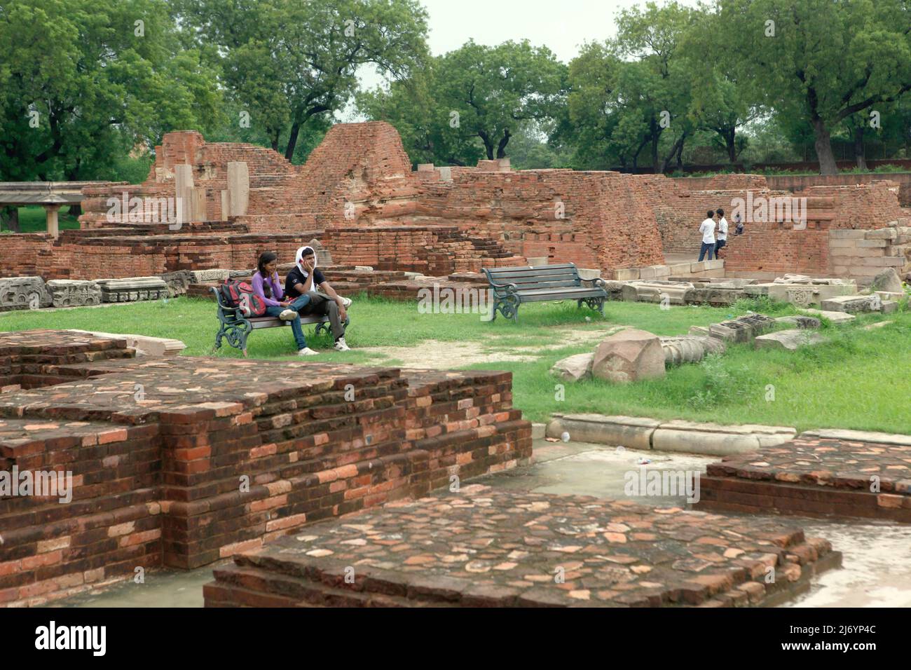 Visitors sitting on a bench in the middle of ruins of brick structures ...