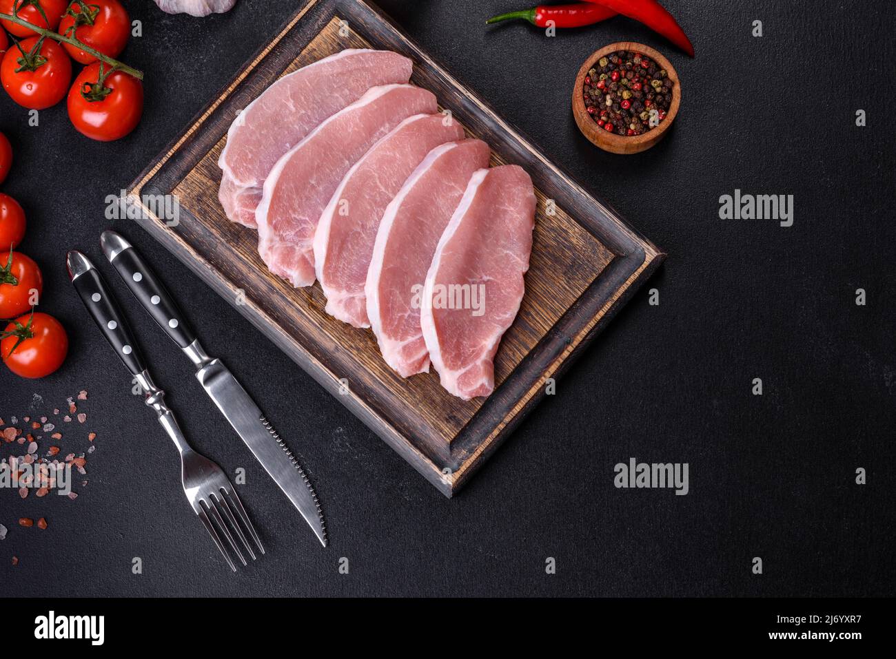 Raw fresh pork meat sliced on a wooden cutting board against a dark ...