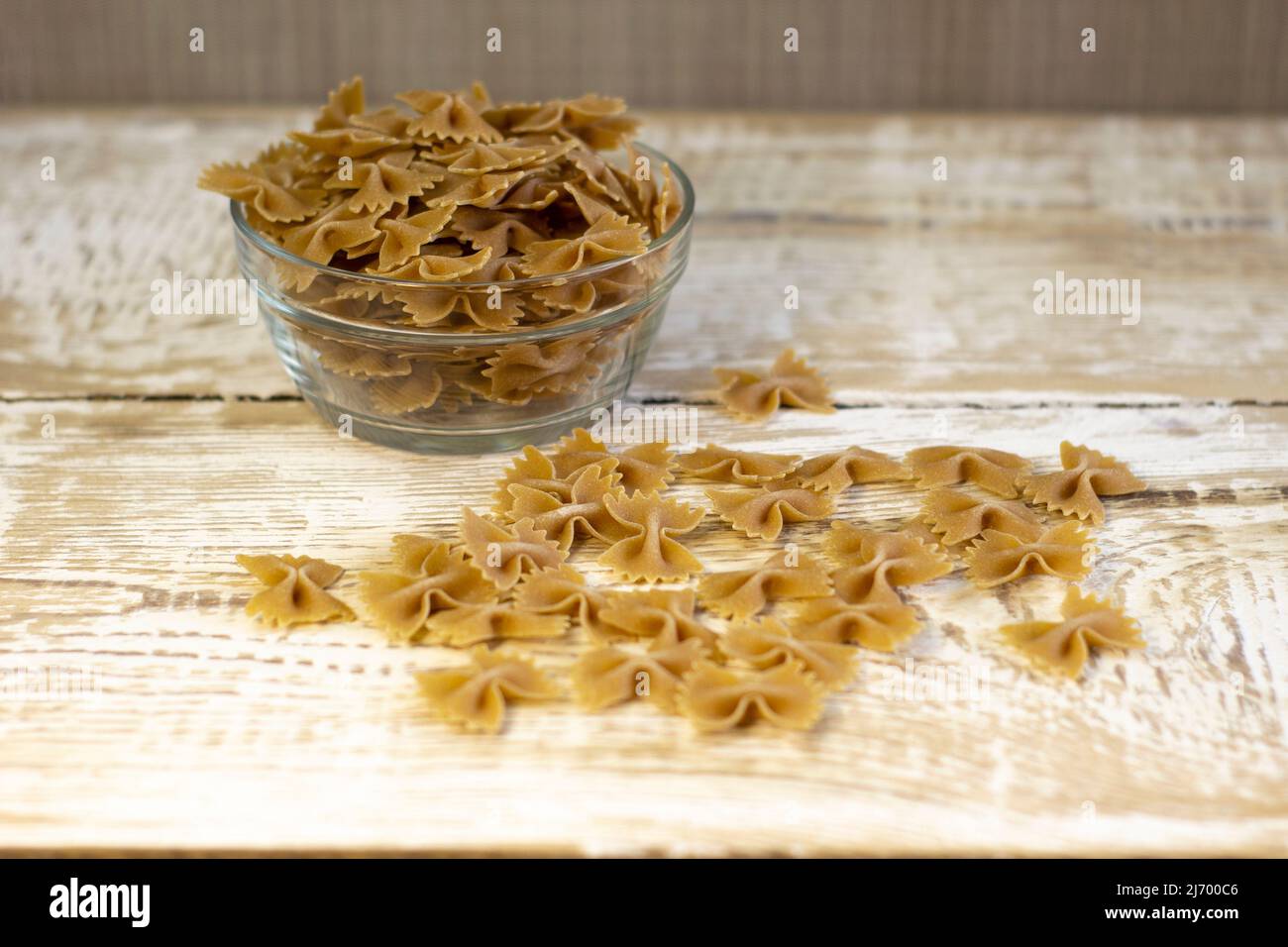 Whole grain dark pasta bows on brown plate on a rough wooden light ...