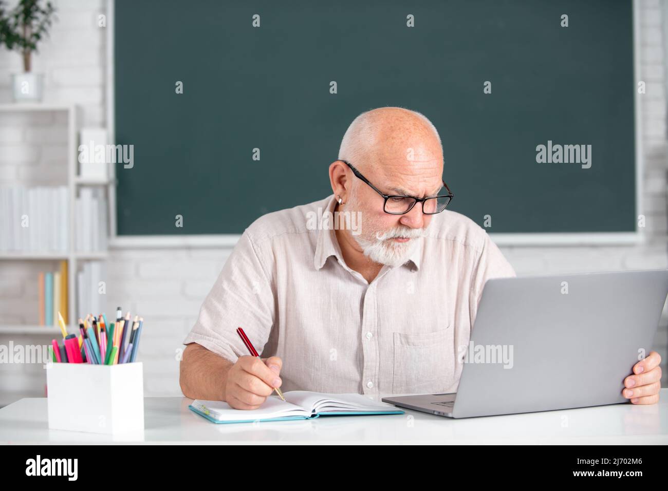 Senior teacher in classroom at university or college. Male old student ...