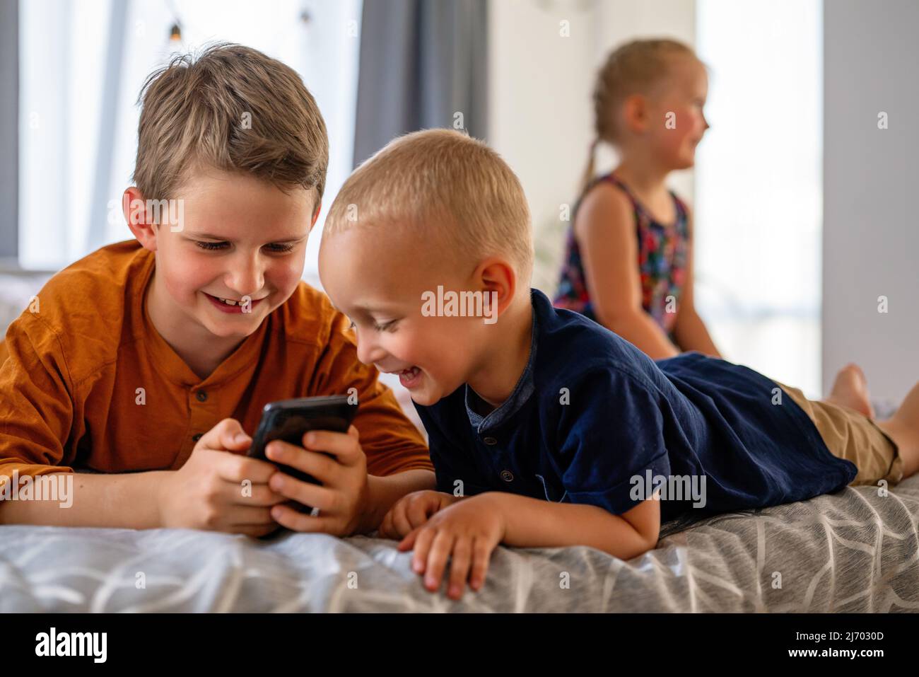 Portrait of children playing on mobile phone together at home. Internet ...