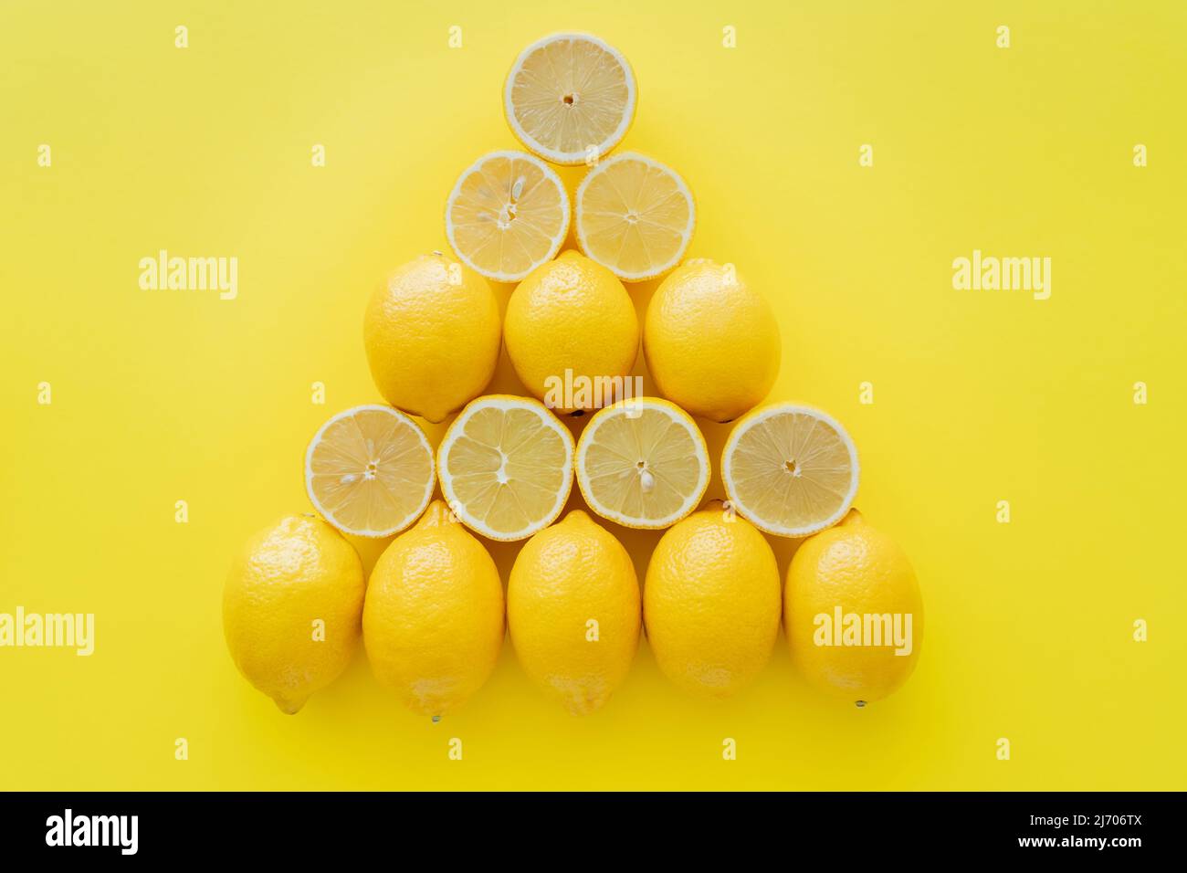 Flat lay with whole and cut lemons in triangle shape on yellow surface ...