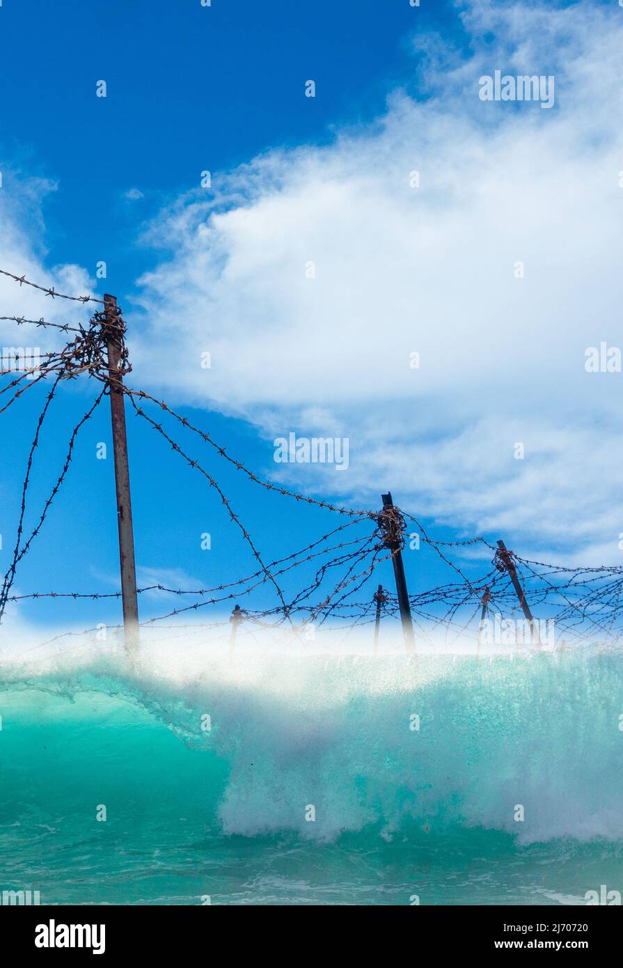 Wave breaking over barbed wire fence. Concept image: sea border ...
