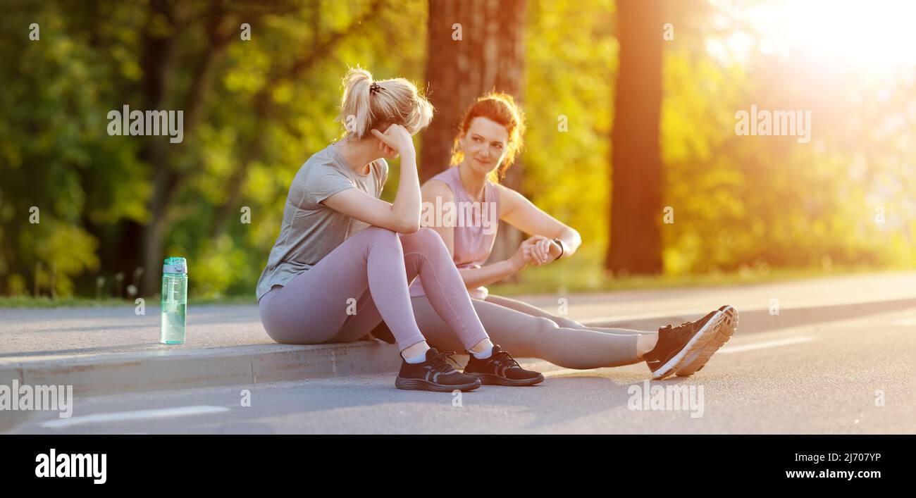 Two women sitting on the border of the roadside after a run. Panoramic ...