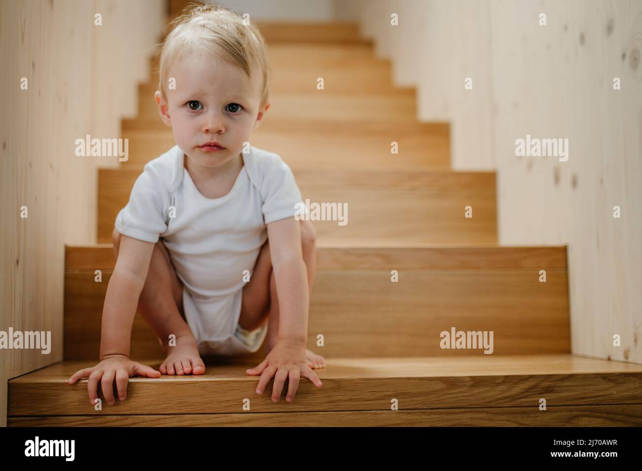 Cute little boy sitting on stairs at home and looking at camera Stock ...