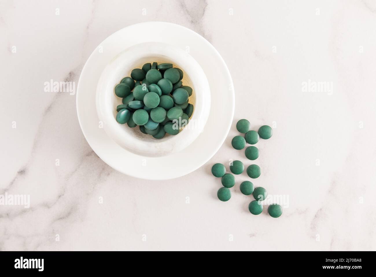 green spirulina algae tablets in a bowl on a white marble table. top ...