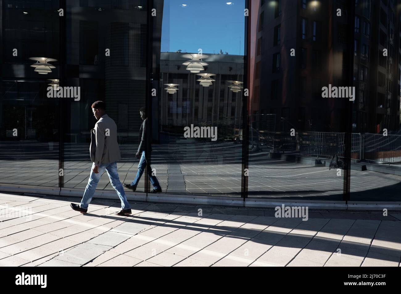 Young Afro-American going along sidewalk past modern office building ...