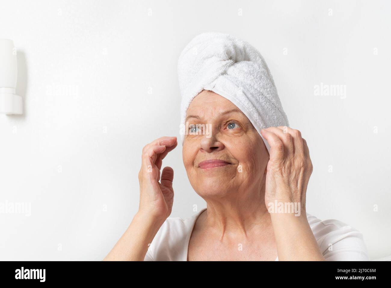 Caucasian senior woman with wrinkles with white towel takes care of her ...
