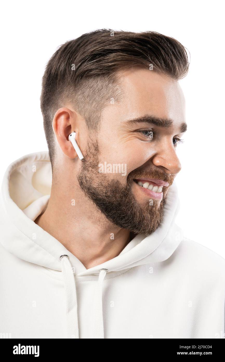 Handsome bearded man in white clothes using wireless earbuds on white ...